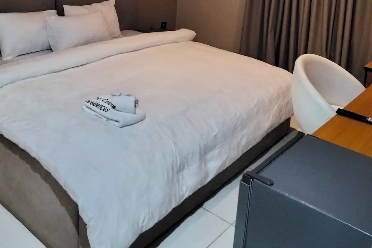 Quarto de hotel com uma cama, uma cadeira, uma escrivaninha e um aparelho de ar condicionado na parede.
