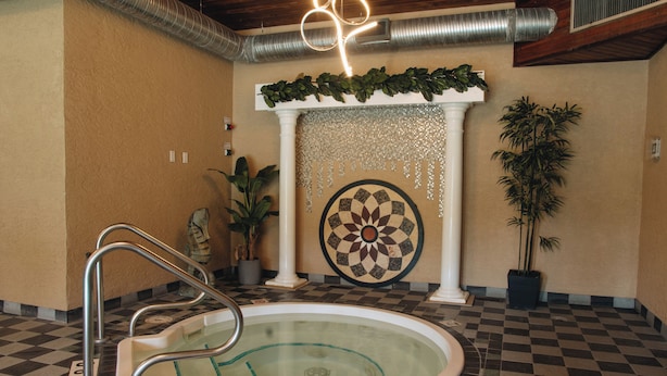 Uma área de spa com hidromassagem, parede decorativa com padrão circular e placa com a mensagem 'NÃO MERGULHAR'.