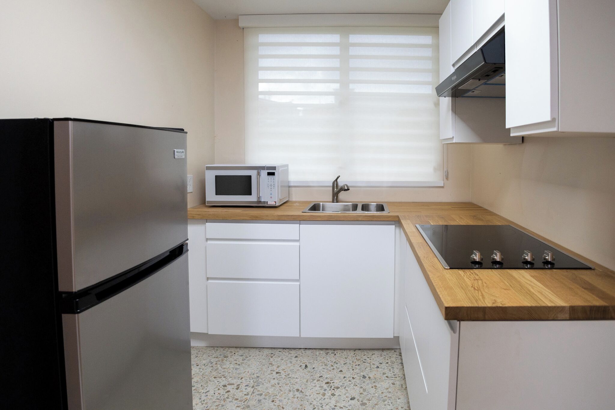 Cozinha compacta com geladeira de aço inoxidável, micro-ondas, pia e bancada de madeira.