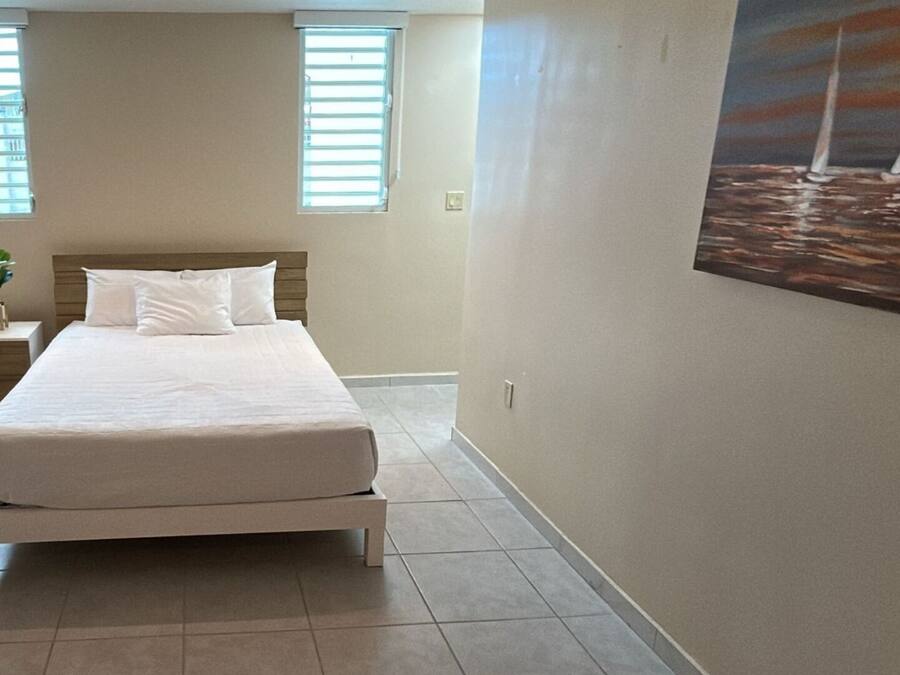 Um quarto com uma cama, uma mesa de cabeceira, uma planta em vaso e um quadro de veleiros na parede.