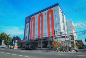 Um hotel com fachada em vermelho e azul bem visível, várias varandas e céu claro.
