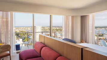 Quarto de hotel moderno com uma varanda grande, um sofá vermelho, uma mesa pequena e vista para a paisagem urbana.
