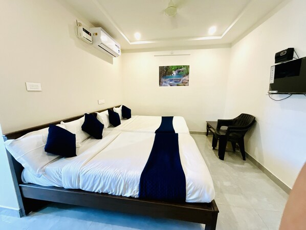 Quarto de hotel com uma cama grande, uma escrivaninha, uma cadeira, aparelho de ar condicionado e TV fixada na parede.