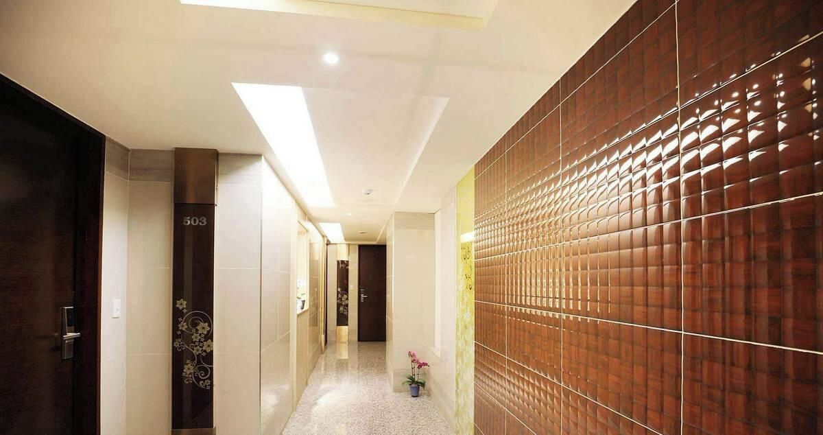 Corredor de hotel com design moderno, apresentando uma parede revestida de azulejos de um lado e uma porta de madeira do outro.