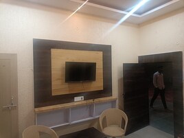 Uma sala de estar moderna com uma televisão de tela plana grande fixada em uma parede de madeira, uma poltrona de vime e uma porta que dá para outro cômodo.
