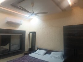 Quarto de hotel com cama, ventoinha no teto, ar condicionado e uma janela grande.