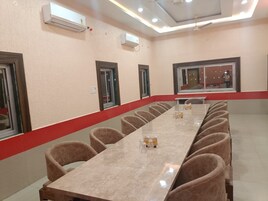 Sala de conferências com uma mesa comprida e cadeiras, unidades de ar condicionado e uma janela com vista.