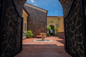 Uma entrada em arco com parede de pedra, uma fonte e um banco.