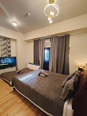 Quarto de hotel com duas camas, televisão de tela plana, luminária no teto e janela com cortinas.