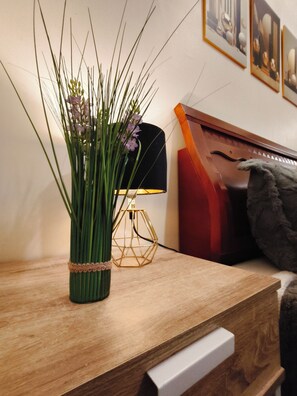 Uma mesa de madeira com um vaso de plantas verdes, uma luminária geométrica e um piano vermelho.