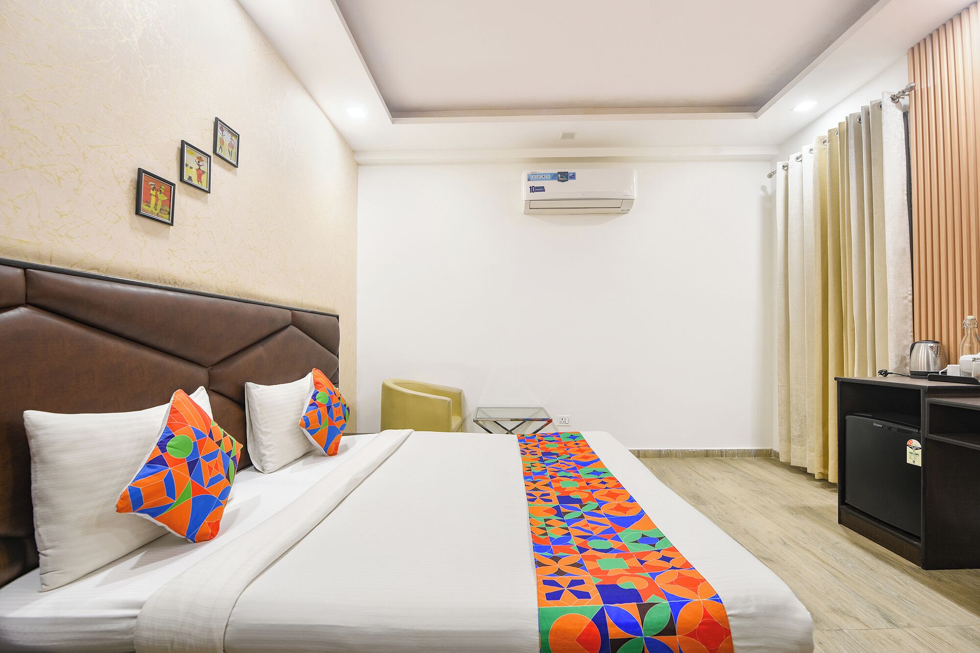 Quarto de hotel com cama, pequena mesa, cadeira, minibar e ar condicionado.