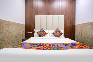 Uma cama com cabeceira branca, duas almofadas com padrões geométricos coloridos e um edredom com estampa geométrica multicolorida.