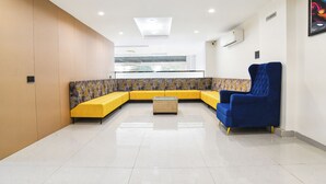 Uma área de espera moderna com um sofá amarelo, uma poltrona azul e uma mesa de centro de vidro.