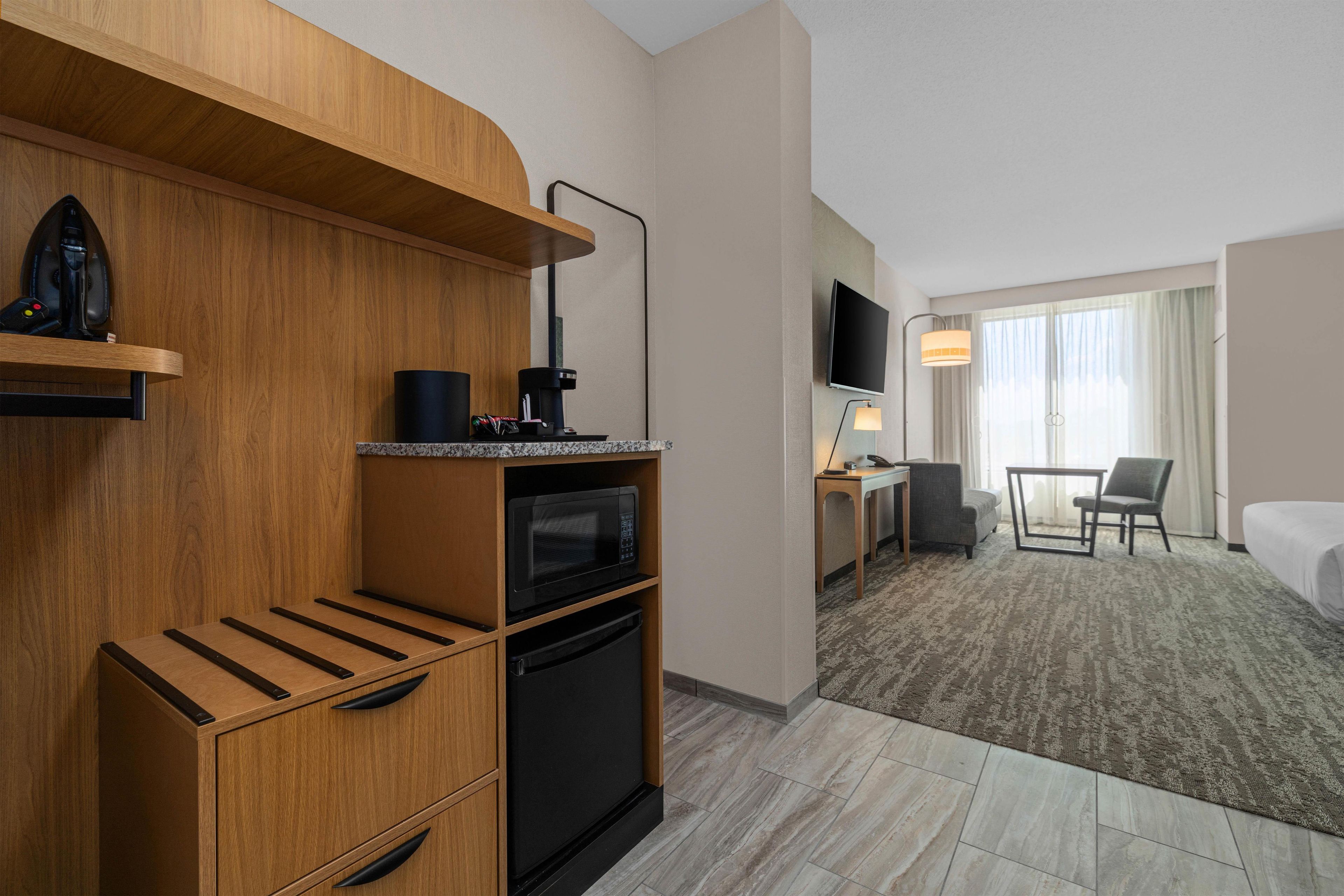 Quarto de hotel com cozinha compacta, TV de tela plana, escrivaninha com cadeira e uma cama.