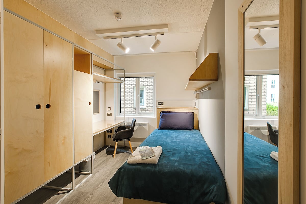 Quarto compacto com cama, escrivaninha e guarda-roupa.