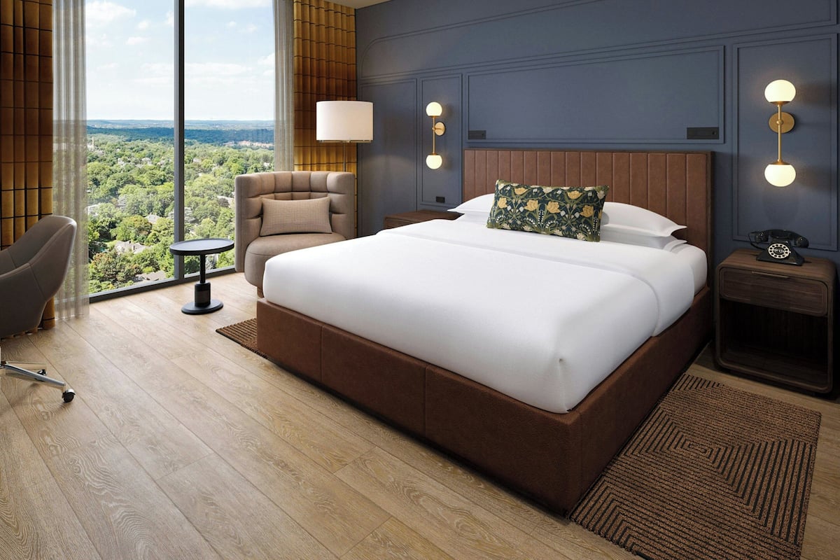 Quarto de hotel moderno com uma cama grande, vista para a cidade, área de estar e uma mesa pequena.