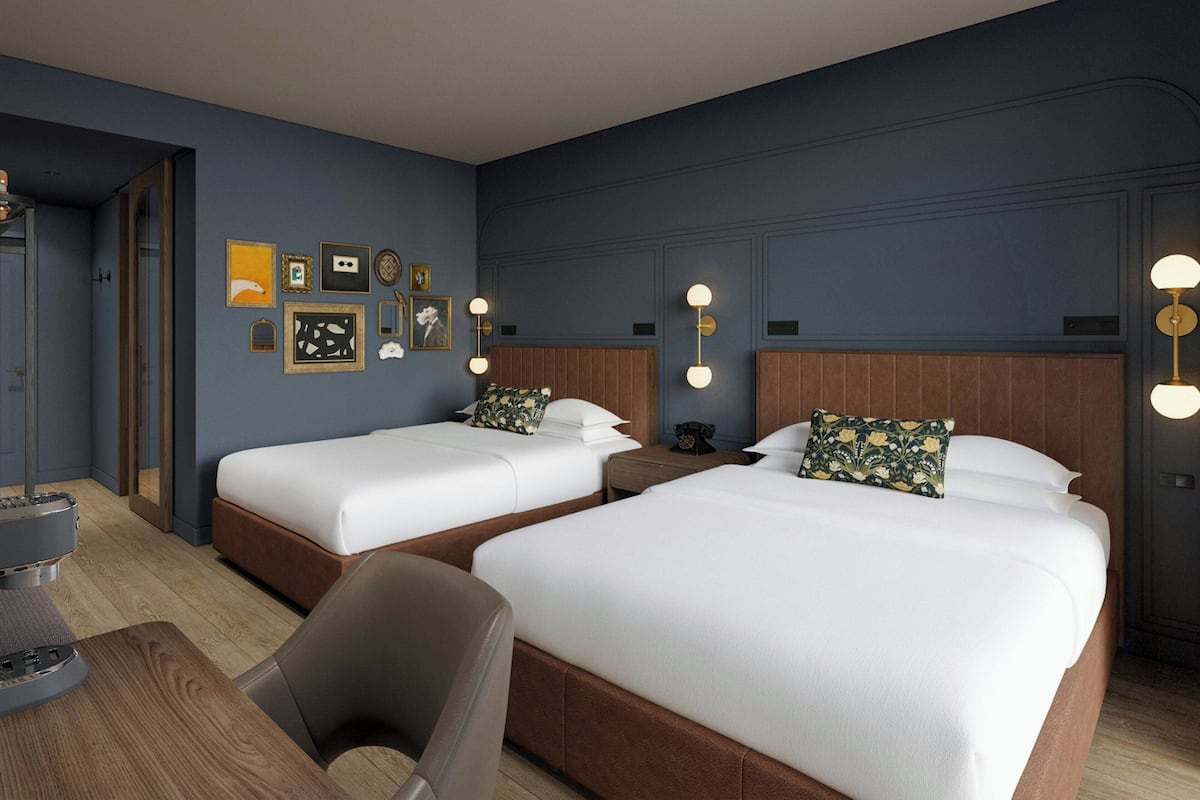 Quarto de hotel com duas camas, uma escrivaninha e uma cadeira.
