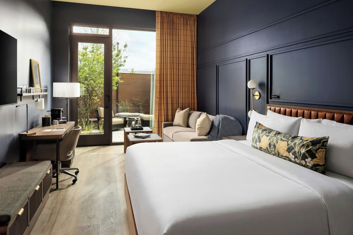 Quarto de hotel com uma cama grande, uma escrivaninha, uma cadeira, um sofá e vista para o exterior.