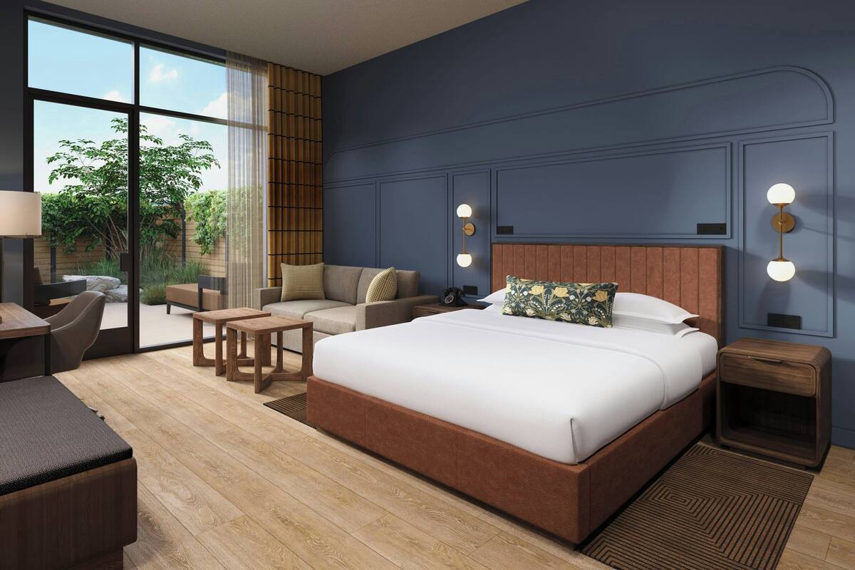 Quarto de hotel moderno com uma cama grande, um sofá, uma mesa de escritório e vista para o exterior.
