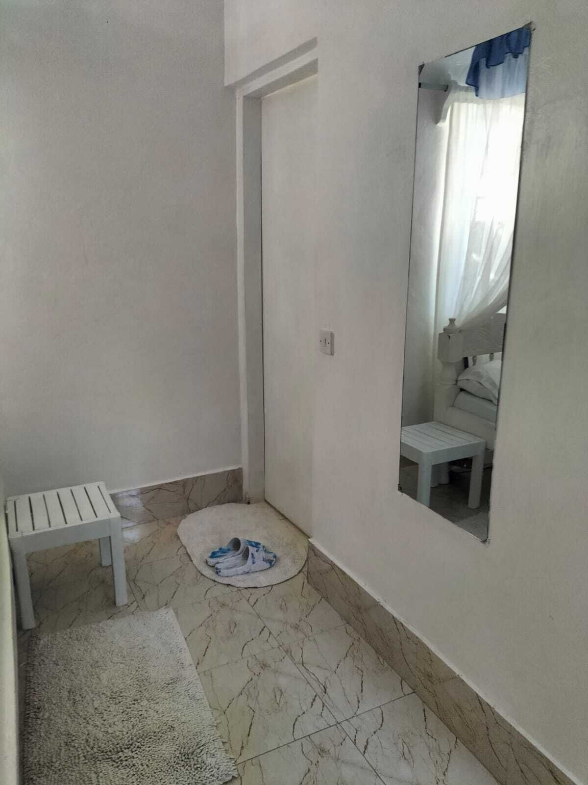 Um banheiro pequeno com um banco branco, um tapete redondo e um espelho na parede.