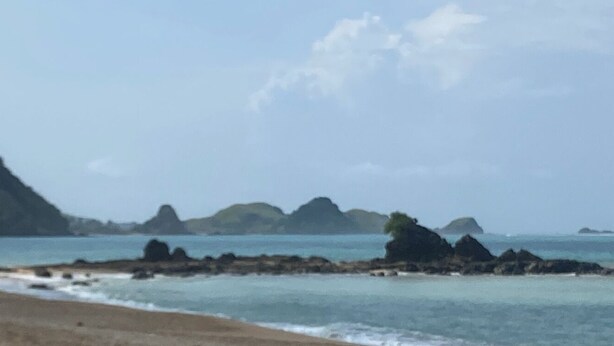 Uma praia com afloramentos rochosos e montanhas ao longe.