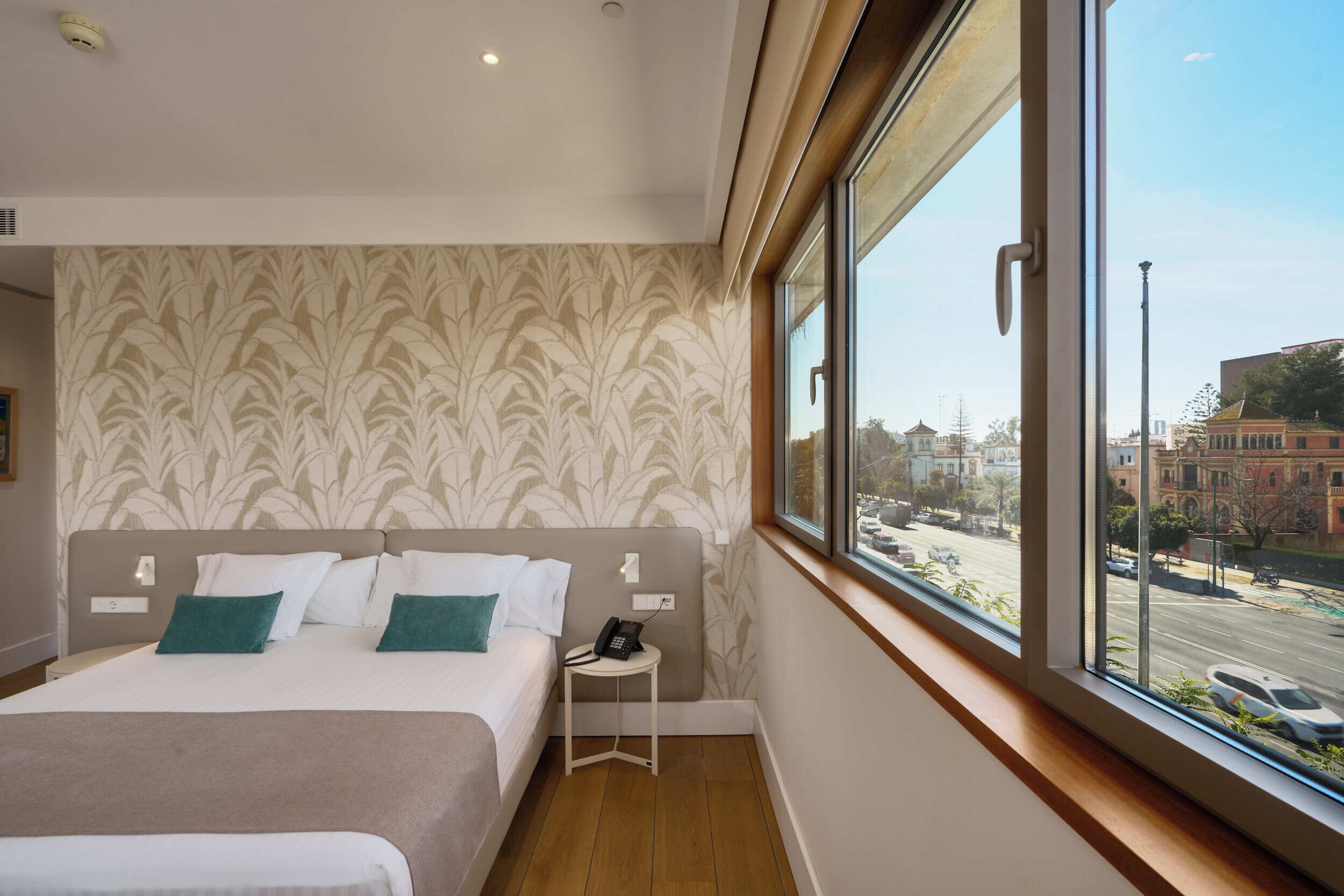 Quarto de hotel com uma cama grande, mesa de cabeceira com telefone e janela com vista para a cidade.