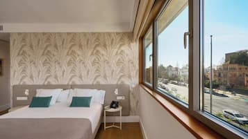 Quarto de hotel com uma cama grande, mesa de cabeceira com telefone e janela com vista para a cidade.