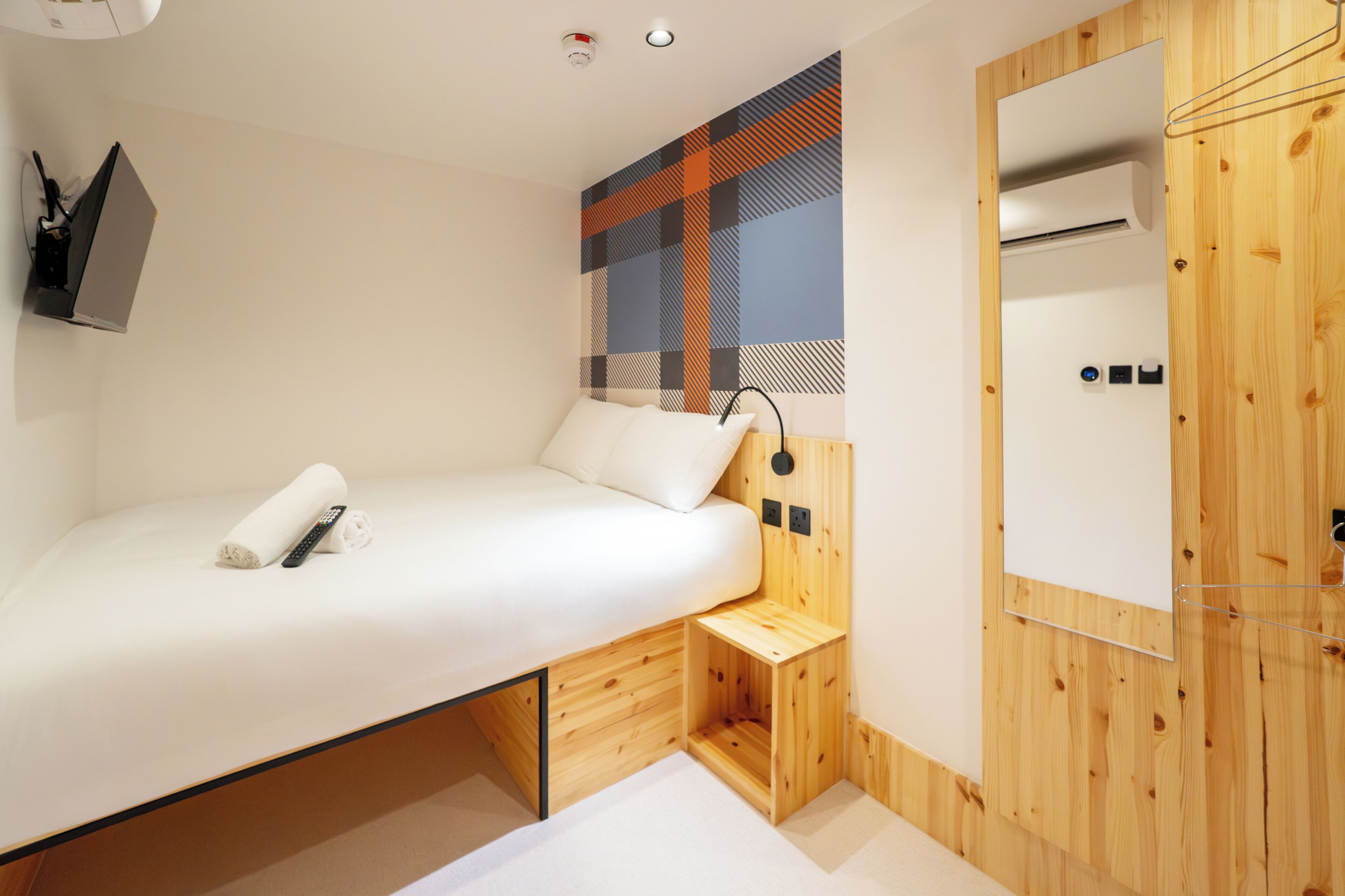 Quarto moderno com cama, mesa de cabeceira de madeira, televisão na parede e guarda-roupa embutido.