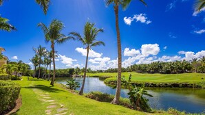 Um campo de golfe com lago, palmeiras e céu azul límpido.