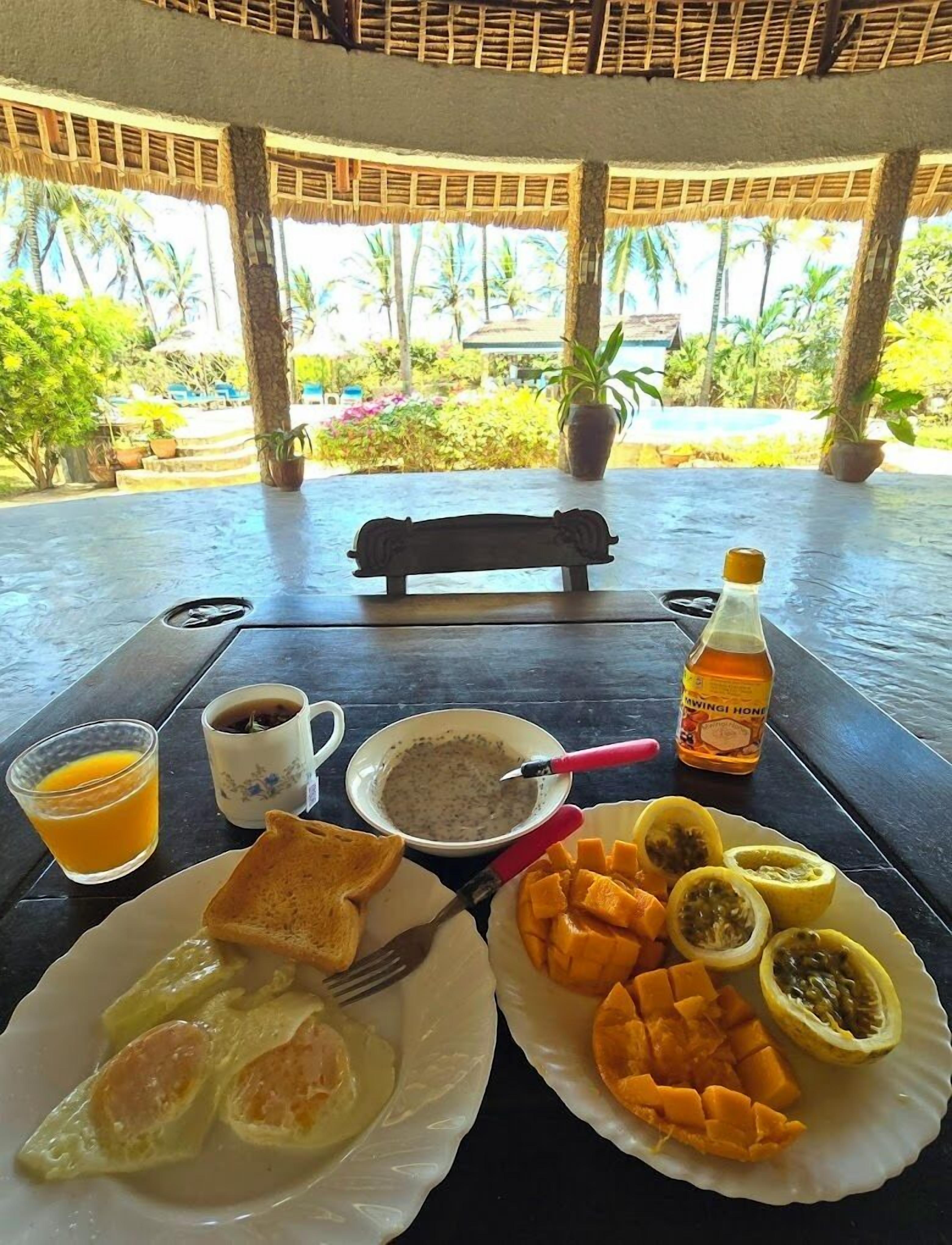 Uma mesa de café da manhã com torradas, ovos, frutas, uma xícara de café e um pote de mel.
