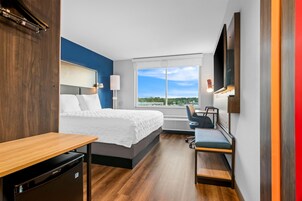 Quarto de hotel com cama, escrivaninha, cadeira e uma grande janela com vista.