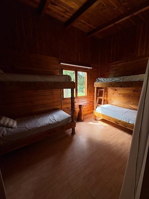 A cabin with two bunk beds, a window, and a wooden floor.