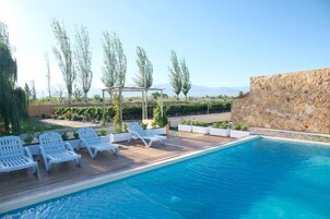 Piscina com espreguiçadeiras, um pergolado e um muro de pedra.