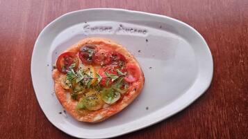 Um prato branco com uma pequena pizza coberta de tomate, ervas e, possivelmente, queijo, sobre uma mesa de madeira.