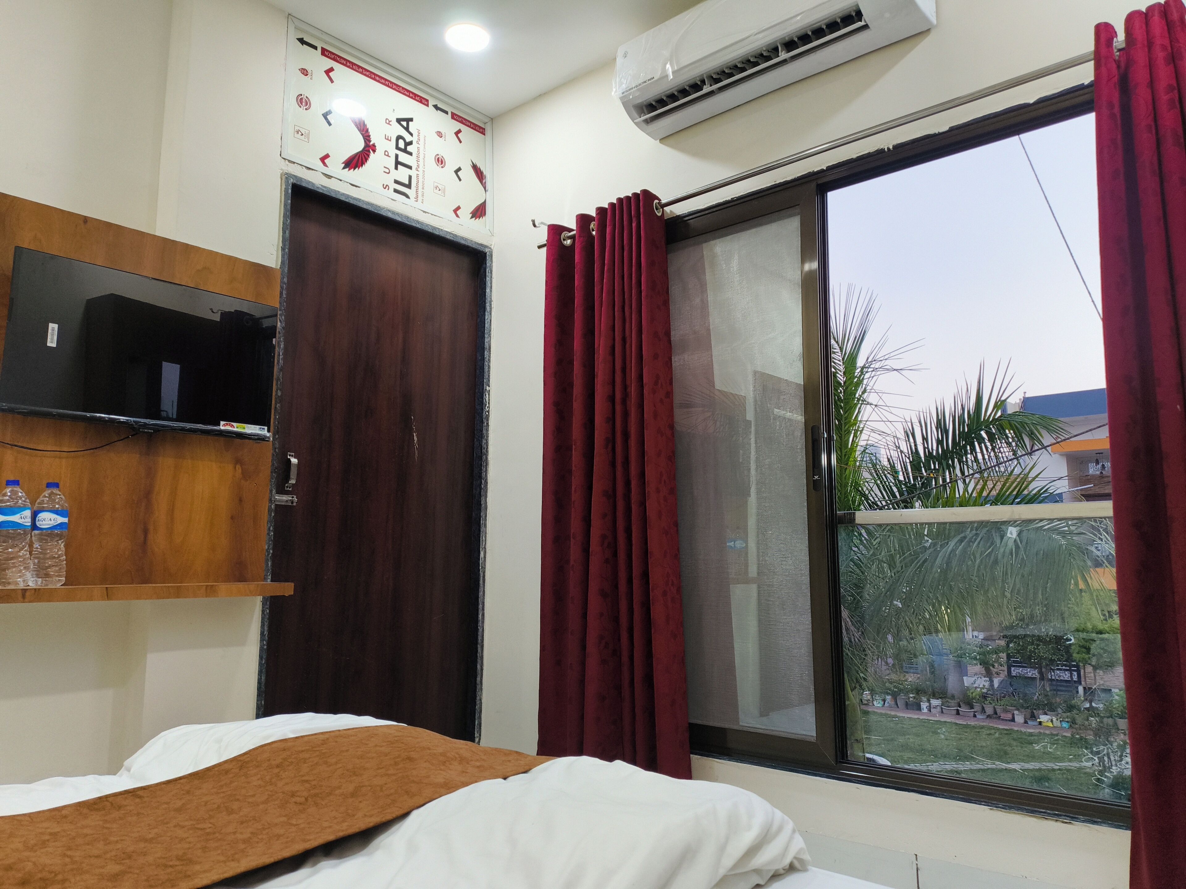 Quarto de hotel com cama, televisão na parede, ar condicionado, janela com cortinas e vista para o exterior.