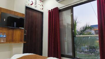 Quarto de hotel com cama, televisão na parede, ar condicionado, janela com cortinas e vista para o exterior.