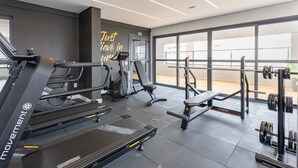Uma academia com esteira, bicicleta ergométrica e banco de musculação.