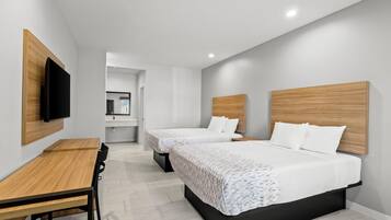 Quarto de hotel moderno com duas camas, uma secretária de madeira, televisão de tela plana e banheiro visível através de uma porta aberta.