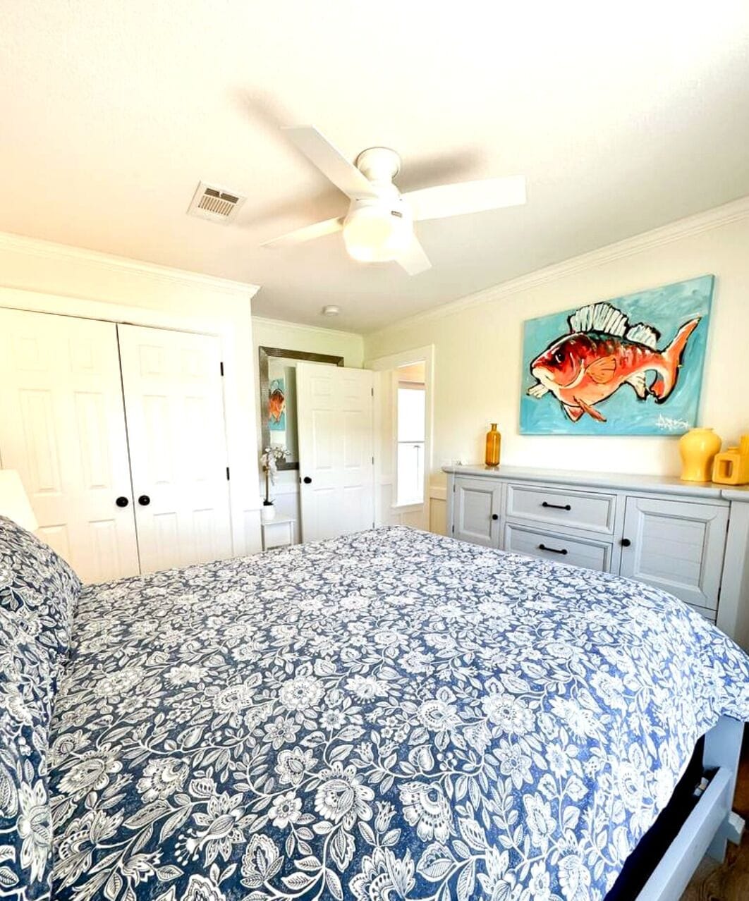 Quarto com cama, ventoinha no teto, pintura de um peixe e cómoda.