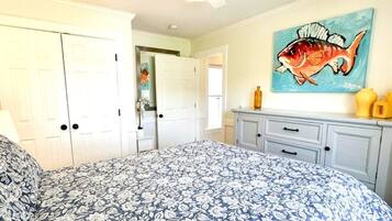 Quarto com cama, ventoinha no teto, pintura de um peixe e cómoda.