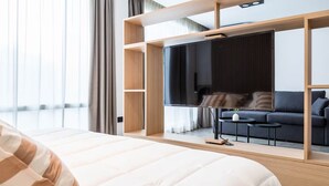 Quarto de hotel com uma cama grande, televisão, sofá e uma mesinha.
