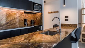 Uma cozinha moderna com bancada de mármore, forno embutido e pia de aço inoxidável.