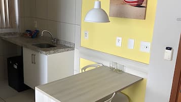 Uma cozinha com bancada de granito, pia, cadeira branca, mesa e luminária pendente.