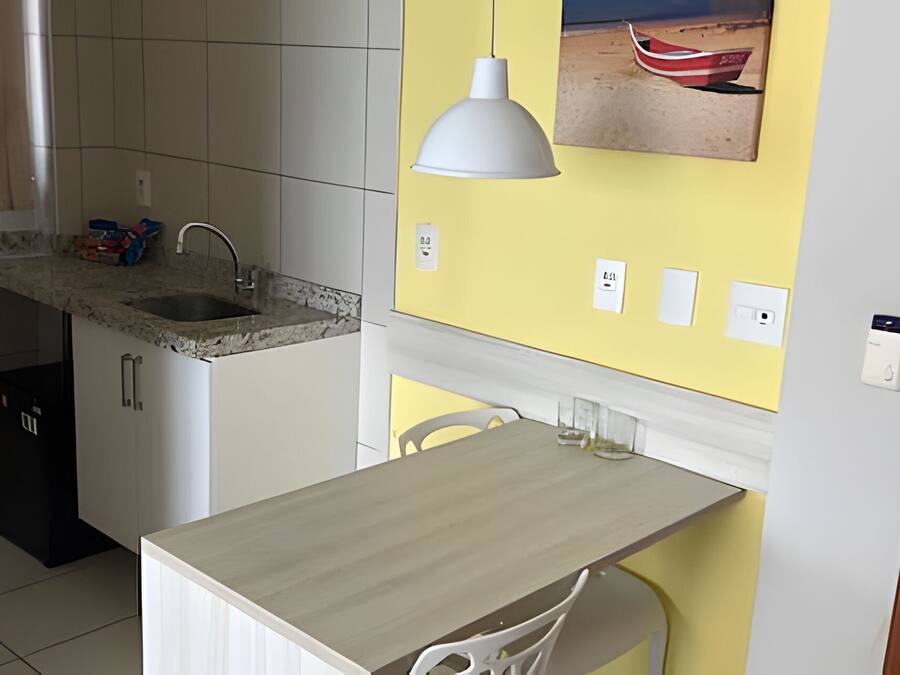 Uma cozinha com bancada de granito, pia, cadeira branca, mesa e luminária pendente.
