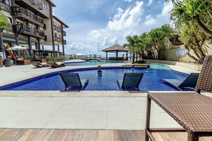 Piscina com espreguiçadeiras, um gazebo e vista para um edifício com sacadas.