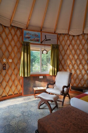 Um quarto acolhedor com parede de madeira treliçada, um banco de madeira, uma poltrona branca e uma mesa pequena.