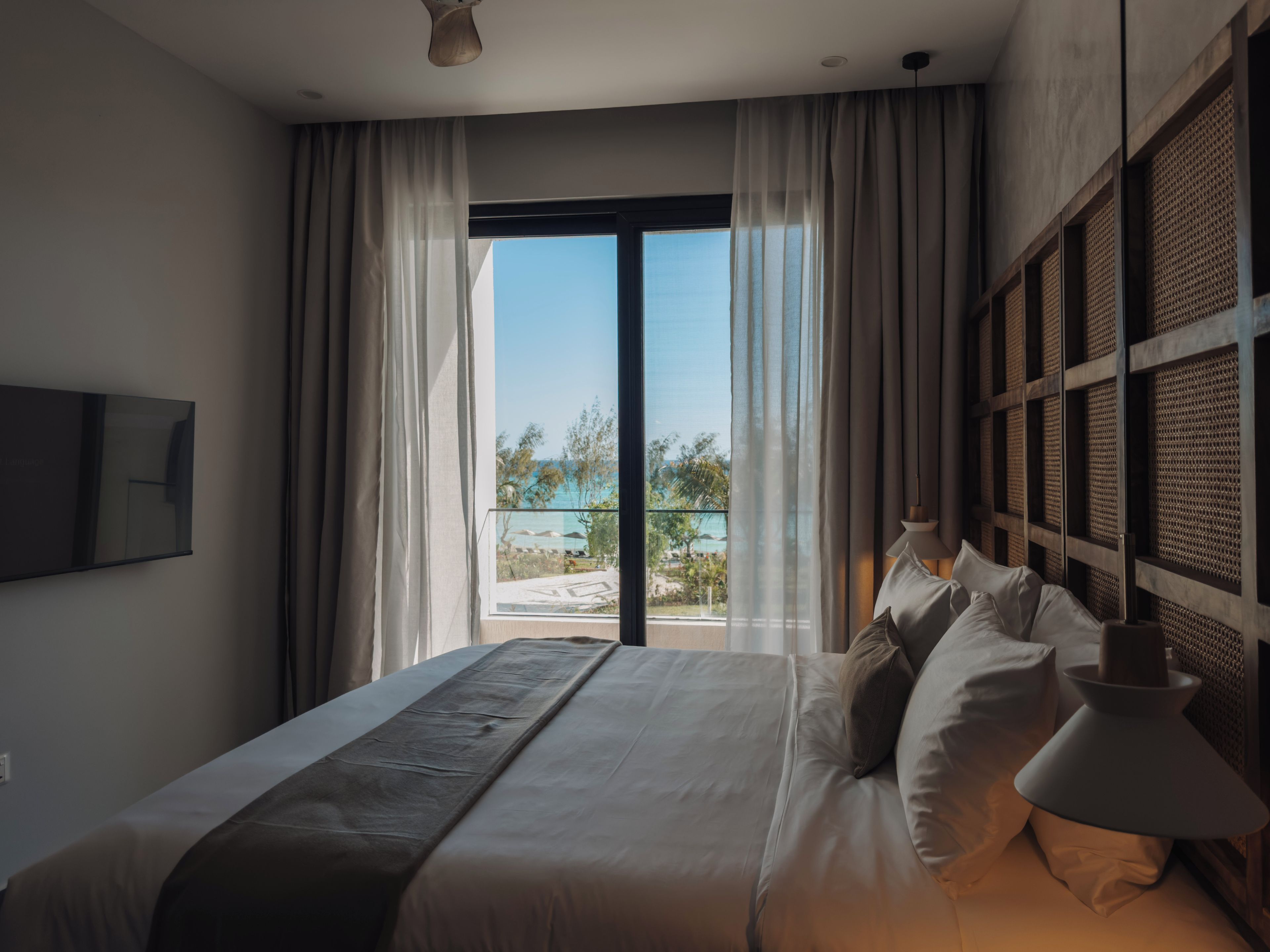 Quarto com cama, cortinas, vista para o exterior e televisão na parede.