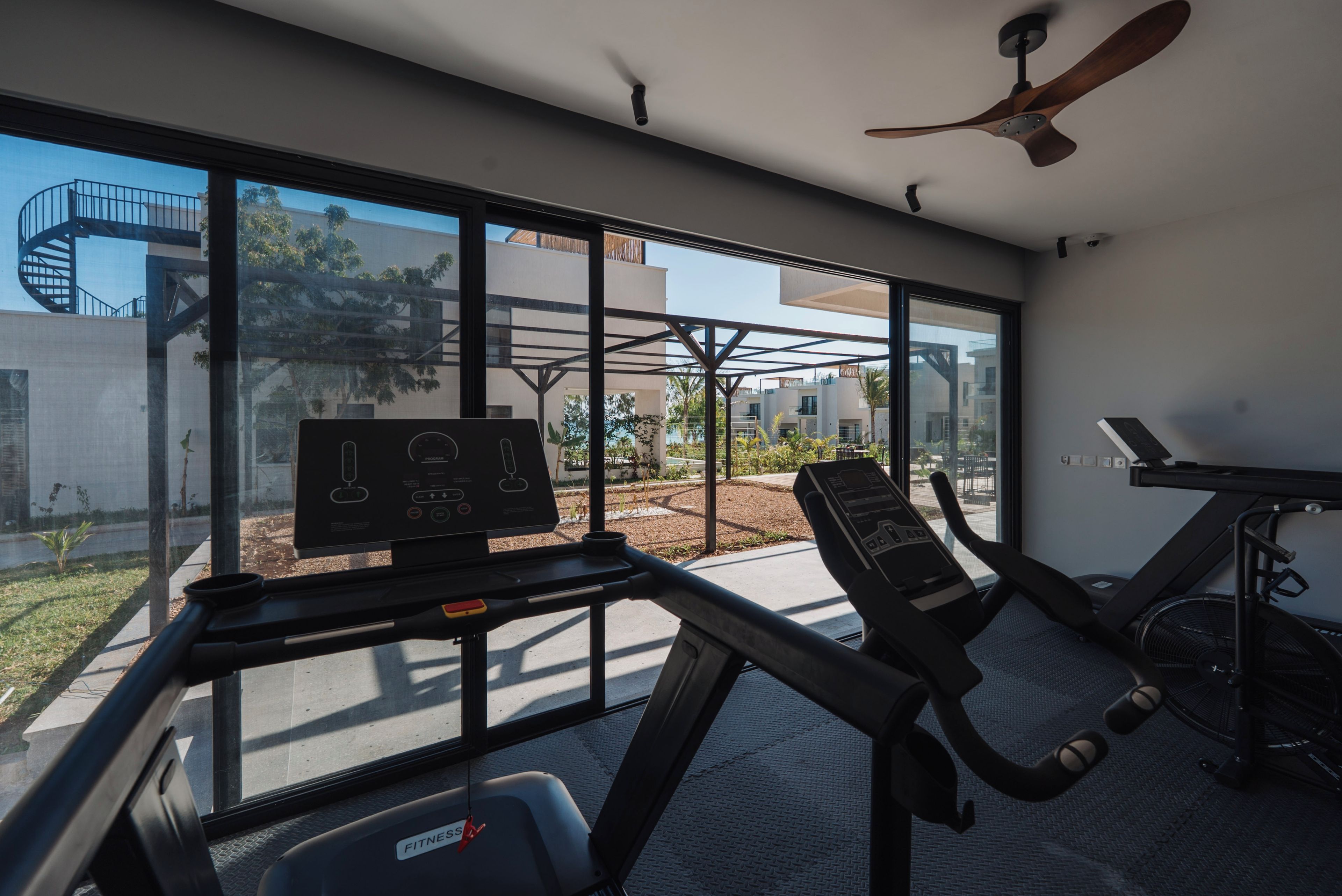 Uma academia moderna com esteira, bicicleta ergométrica e uma grande janela com vista para uma área residencial.