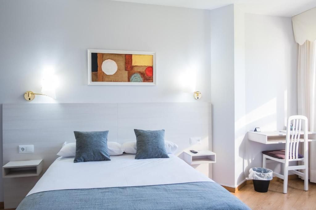 Quarto de hotel moderno com cama, mesas de cabeceira, escrivaninha e uma cadeira.