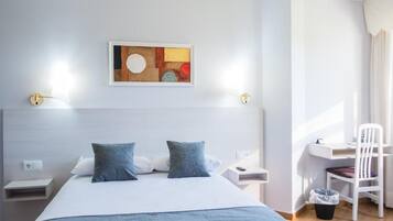 Quarto de hotel moderno com cama, mesas de cabeceira, escrivaninha e uma cadeira.